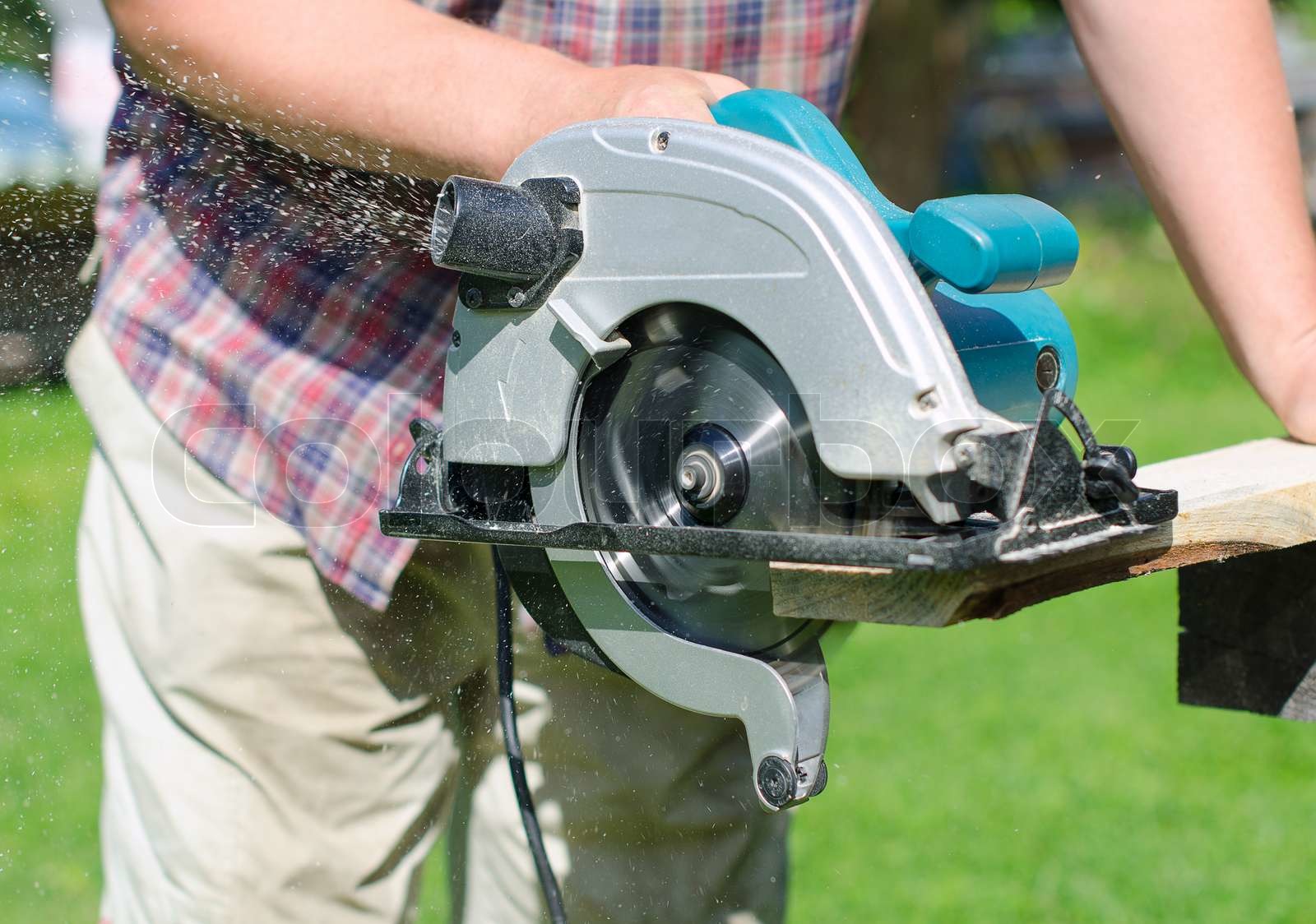 Handyman using hand-held saw machine outdoors | Stock image | Colourbox