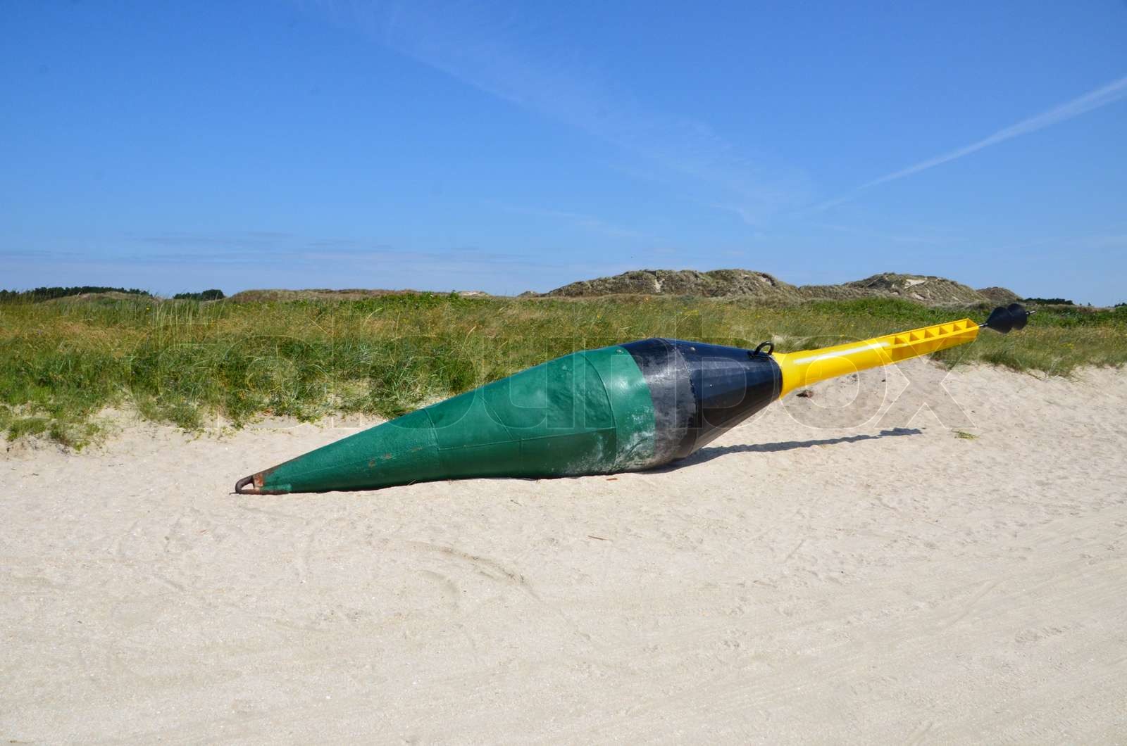 stor bøje i grøn sort og gul farve ligger på hvid sandstrand med klit ...