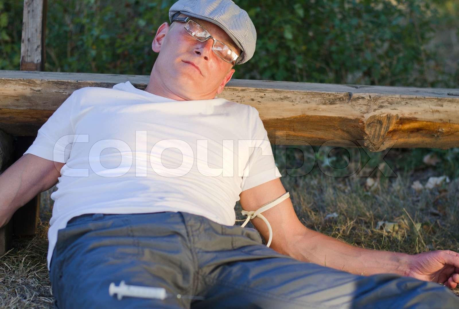 Middle-aged drug addict in a trendy cap and glasses lying slumped ...