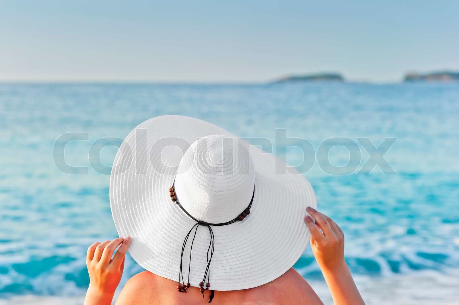 A woman sunbathing on a deck chair on the beach and holding hands hat ...