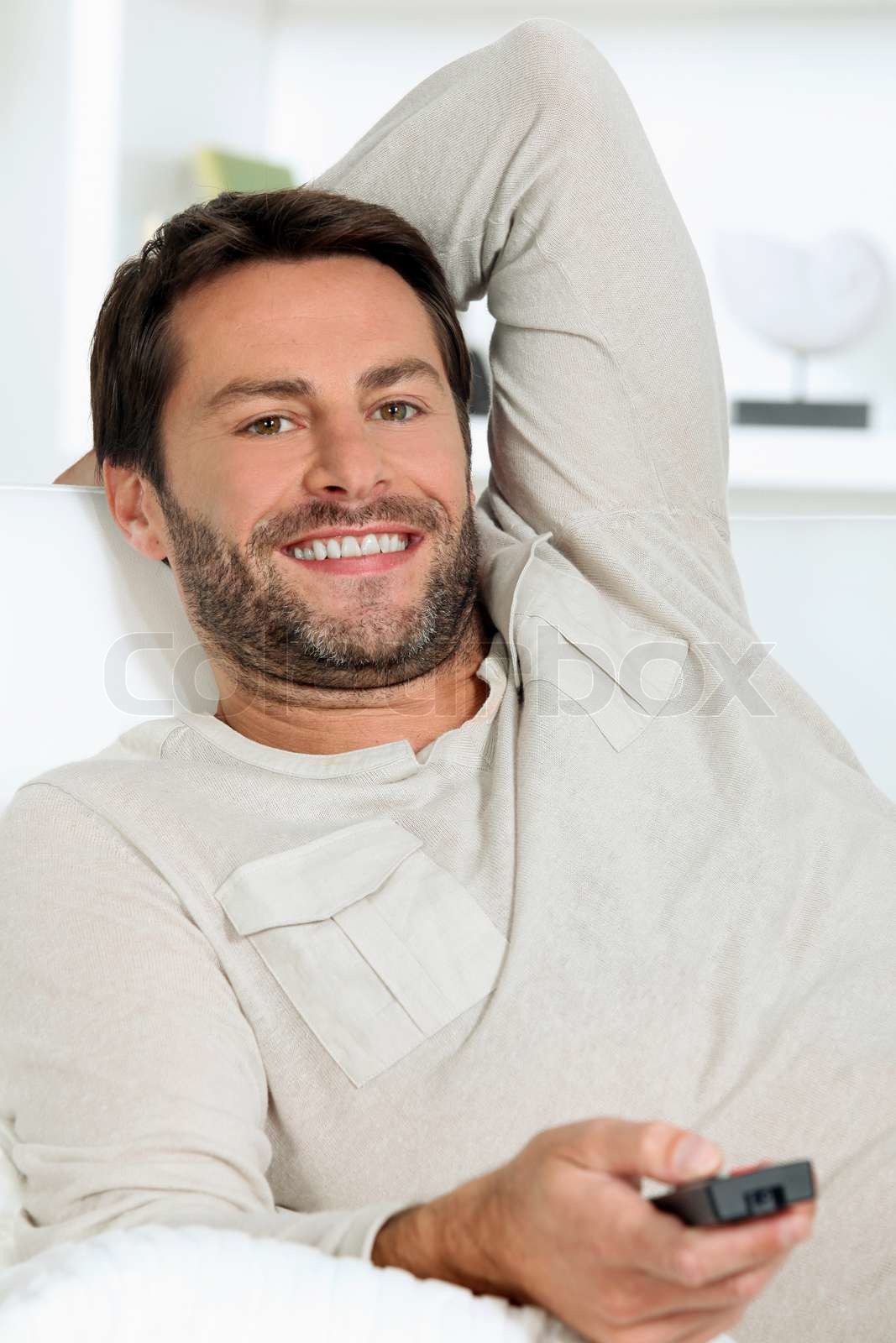 Man watching television in a white room using a remote control | Stock ...