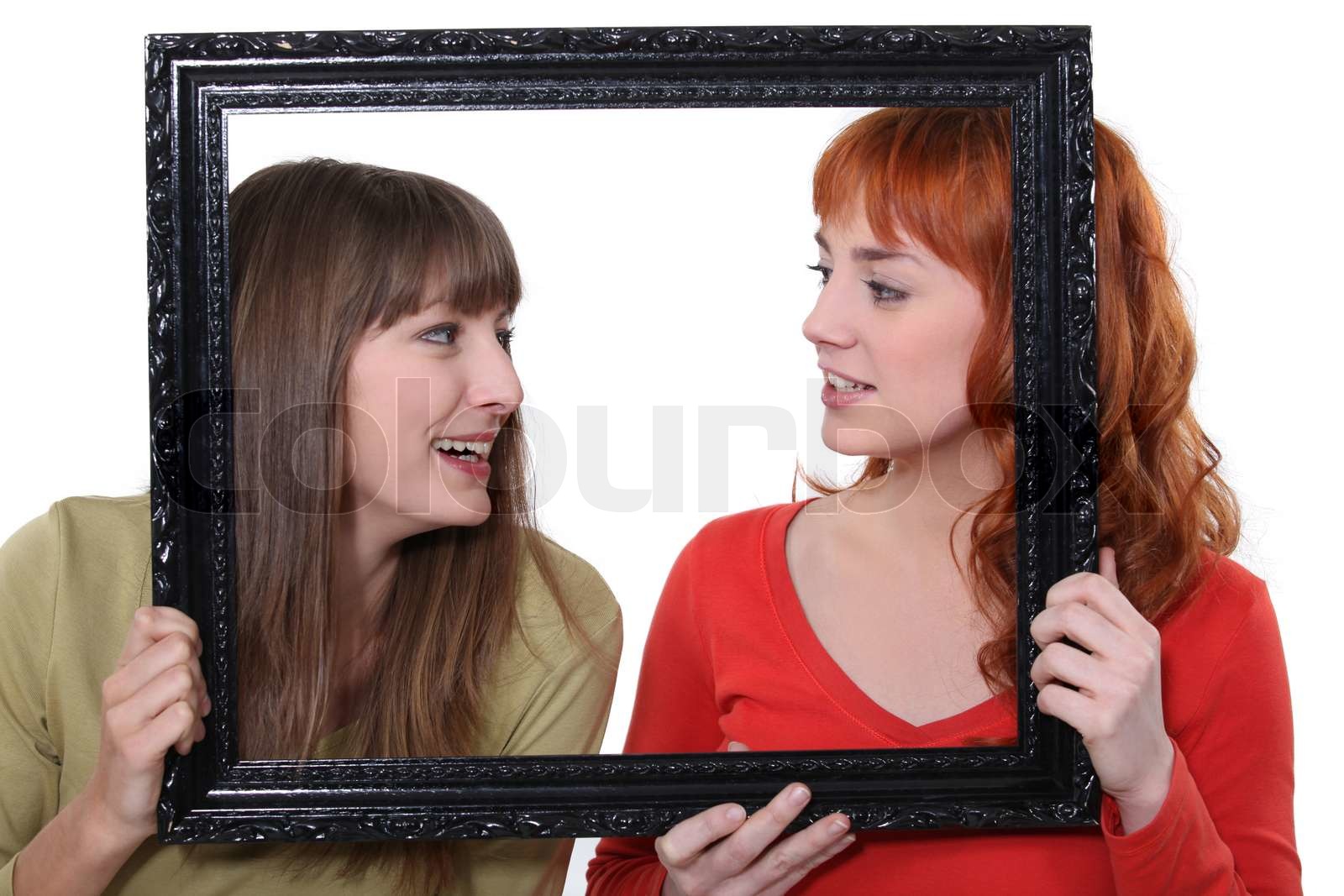 Two women poking heads though empty picture frame | Stock image | Colourbox