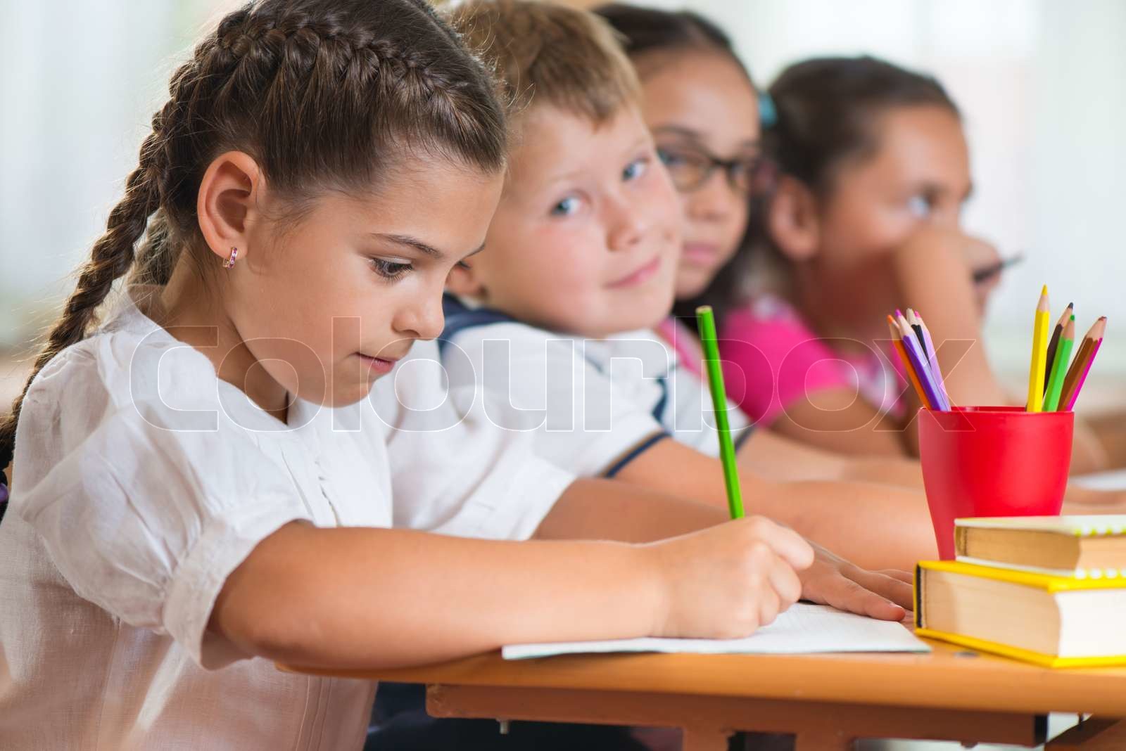 Four diligent pupils sitting in row and studying at classroom | Stock ...