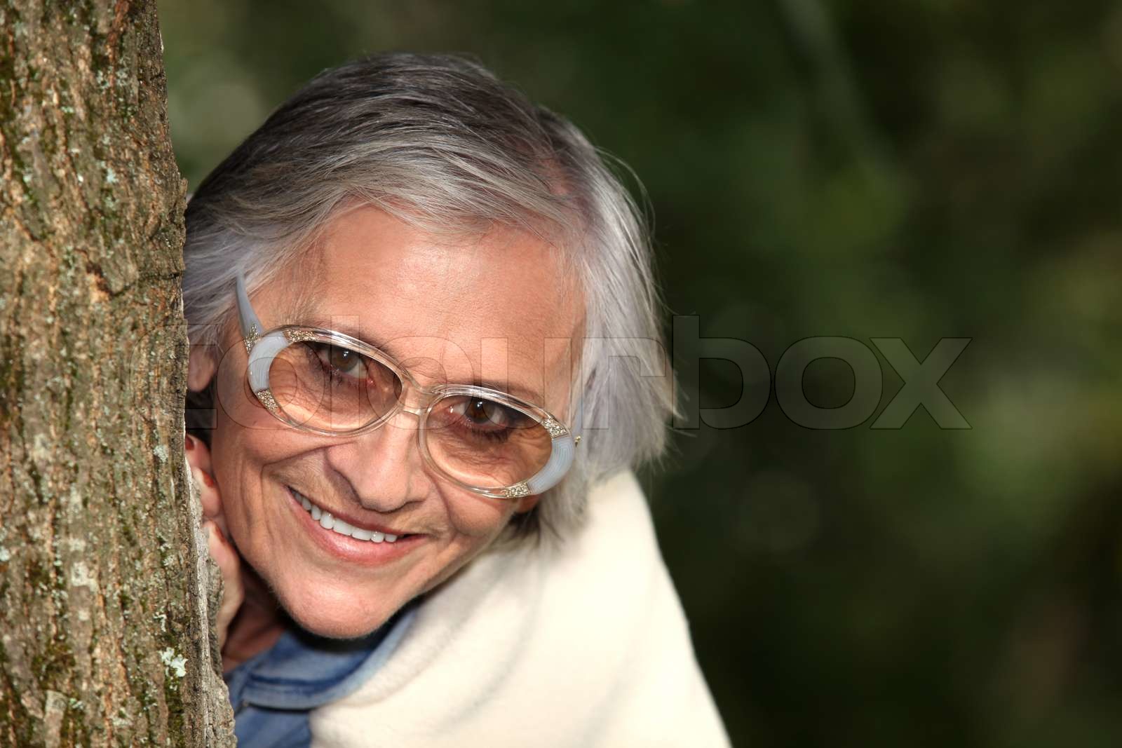 Elderly woman behind tree trunk | Stock image | Colourbox