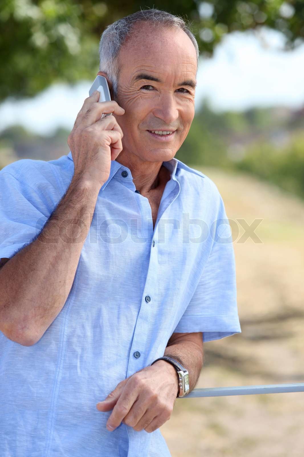 65 years old man at phone in front of a village | Stock image | Colourbox