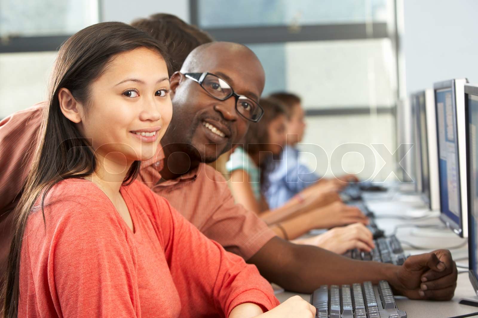 Teacher Helping Students Working At Computers In Classroom | Stock ...