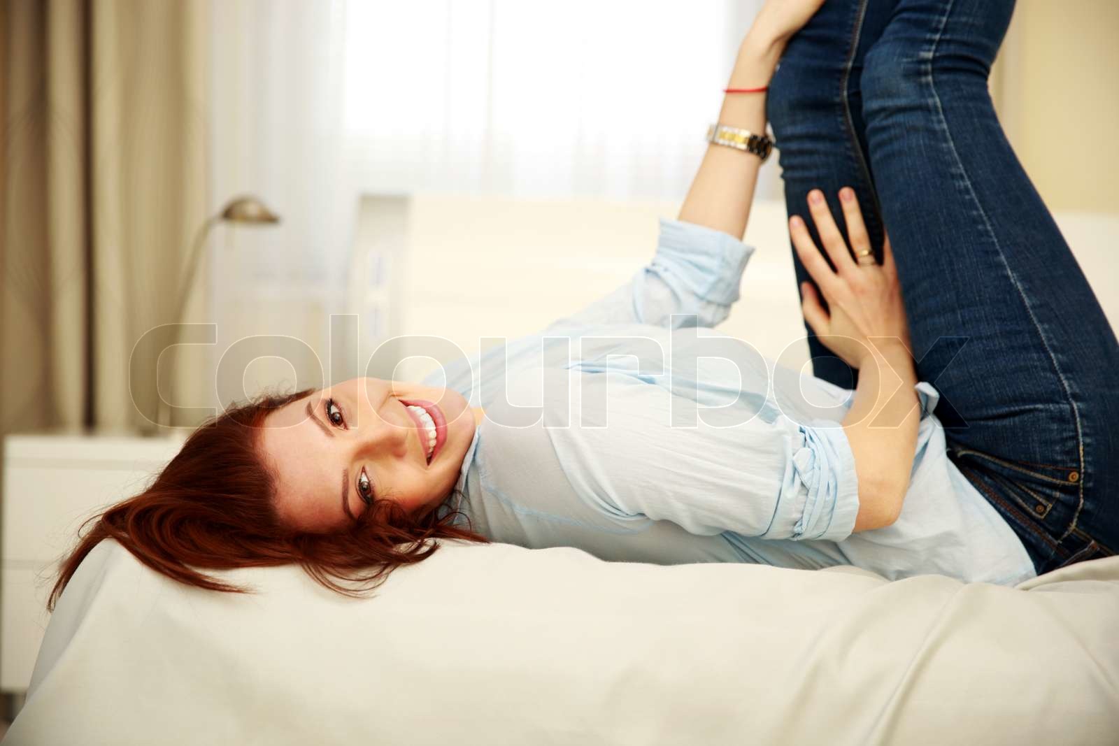 Cheerful woman lying on the bed with raised legs at home | Stock image ...