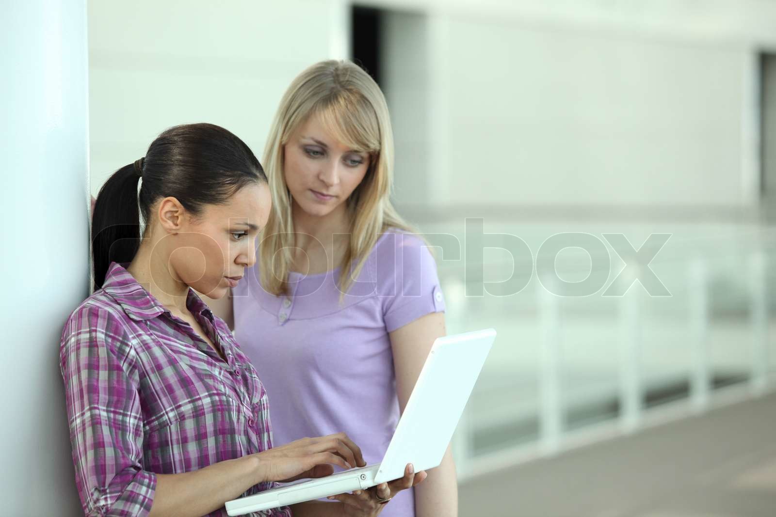 Two girls stood in the a corridor with a computer | Stock image | Colourbox