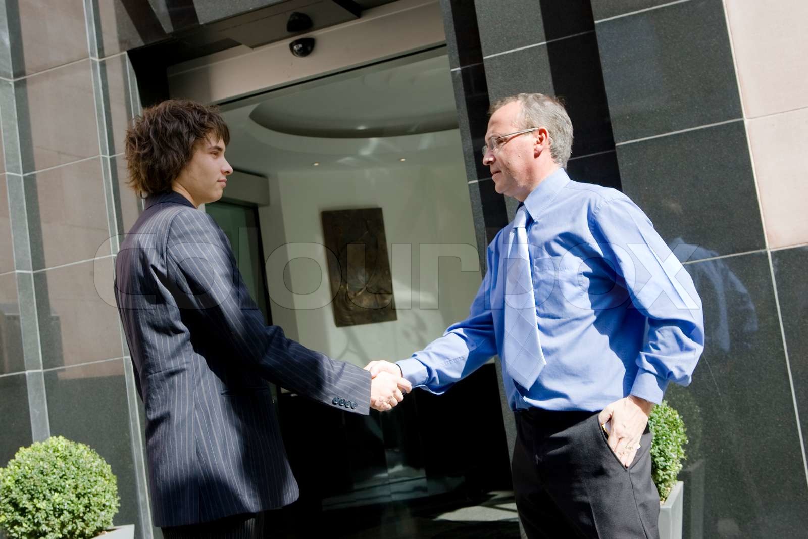 Businessmen shaking hands outside a building entrance | Stock image ...