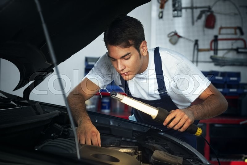 Mechanic looking to car engine and holding lamp | Stock Photo | Colourbox