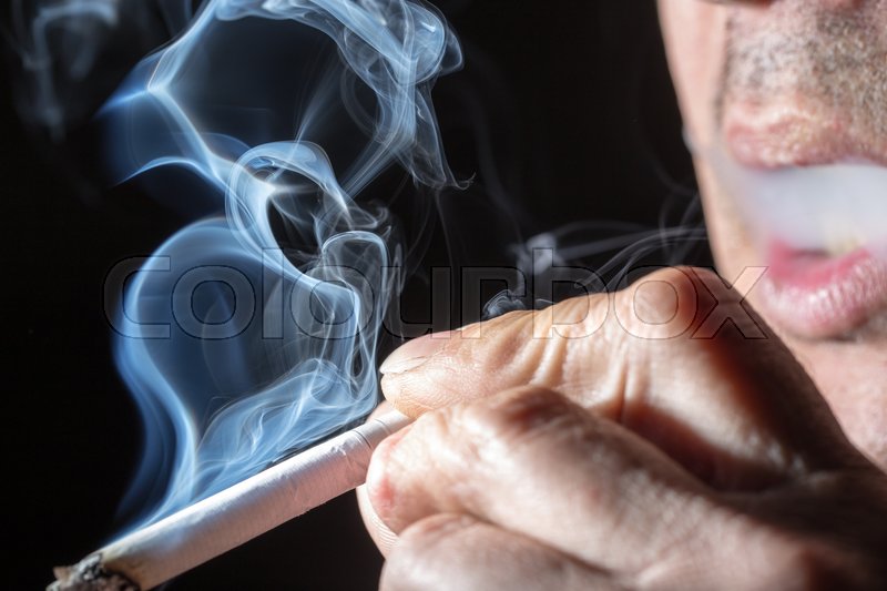 Cigarette smokes in hand on a black ... | Stock image | Colourbox