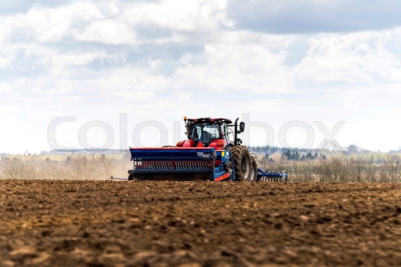 Red tractor driving on a field with a ... | Stock image | Colourbox