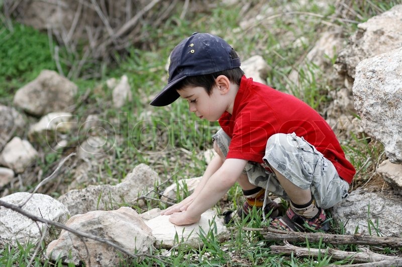 Little boy squatting on stones outdoors | Stock image | Colourbox
