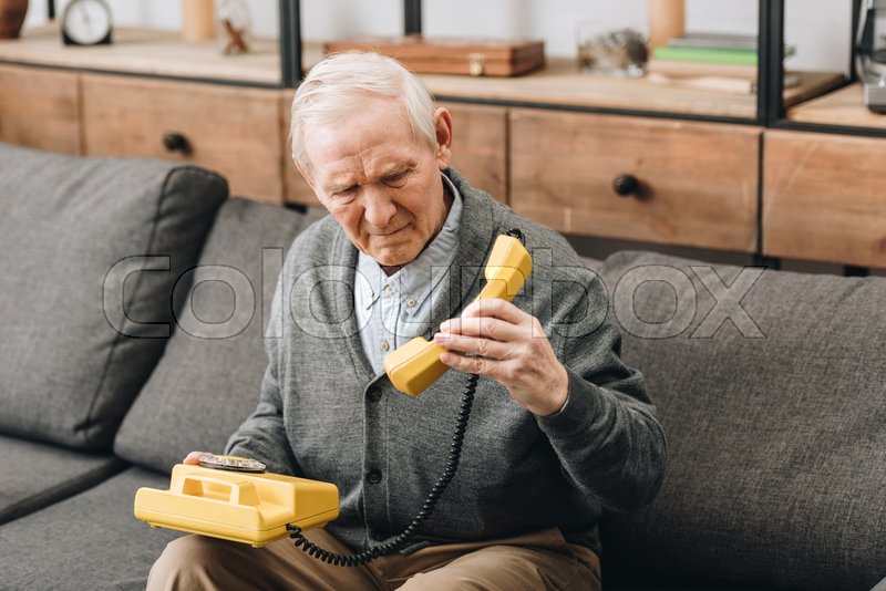 Retired man looking at old phone while ... | Stock image | Colourbox
