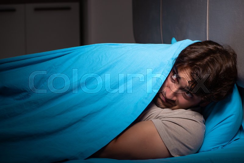 Young man scared in his bed having ... | Stock image | Colourbox