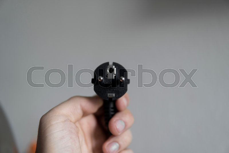 Hand holding black electric plug on a ... | Stock image | Colourbox