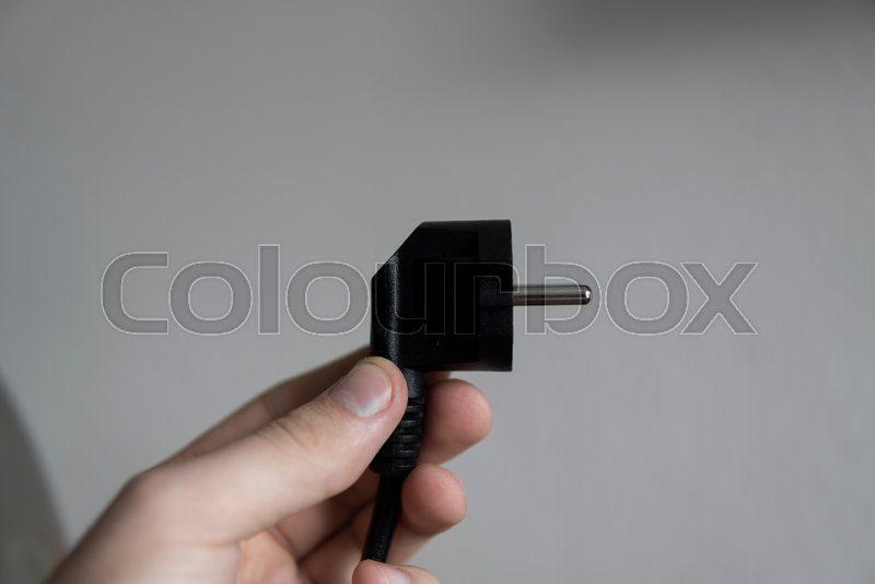 Hand holding black electric plug on a ... | Stock image | Colourbox