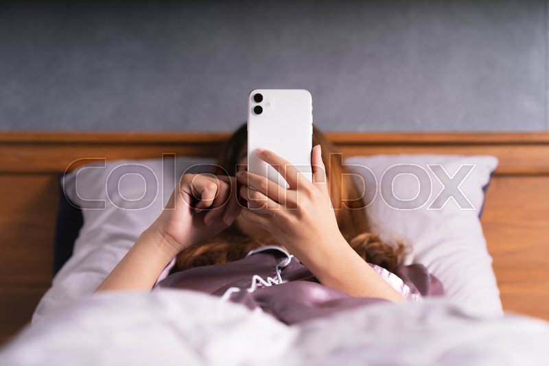 Woman using phone on bed after wake up | Stock image | Colourbox