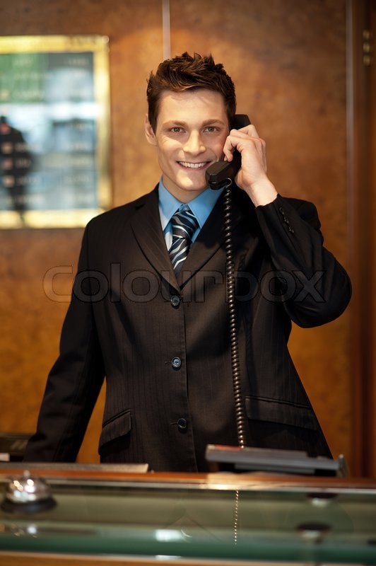 Cheerful front desk executive attending phone call while looking at ...