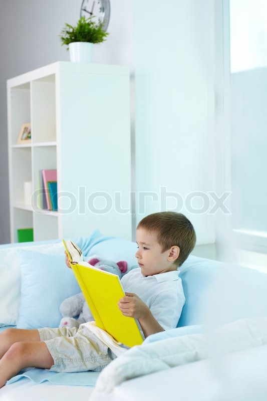 Little kid sitting on sofa and reading ... | Stock image | Colourbox