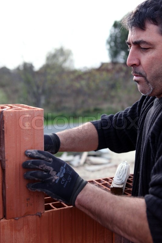 Mason working on unfinished brick wall | Stock Photo | Colourbox